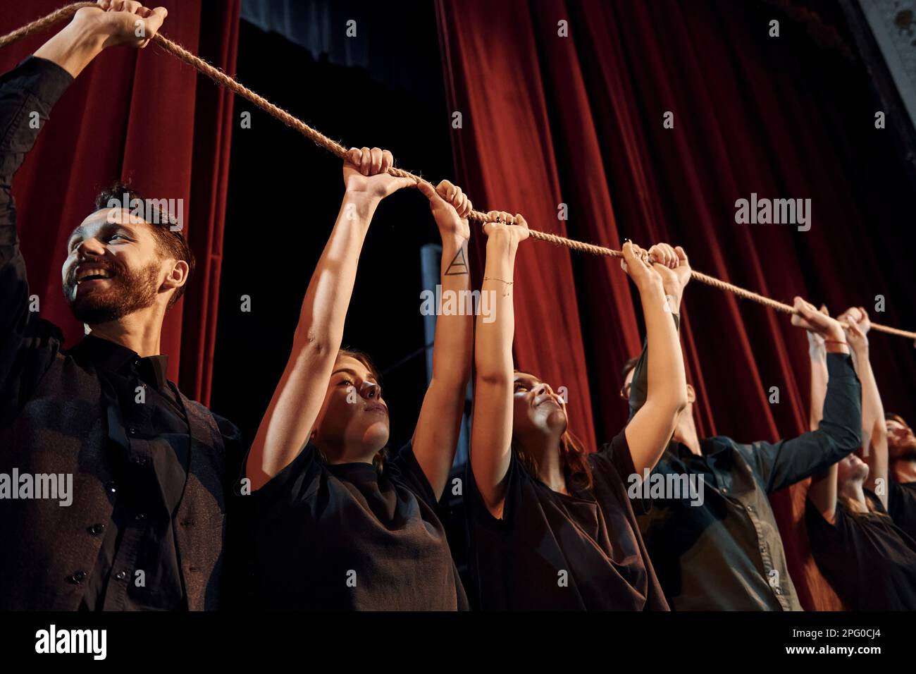 Holding rope in hands above the heads. Group of actors in dark colored ...
