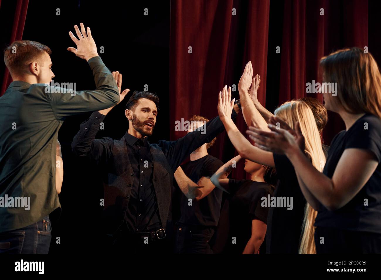 Giving high five, celebrating success. Group of actors in dark colored ...