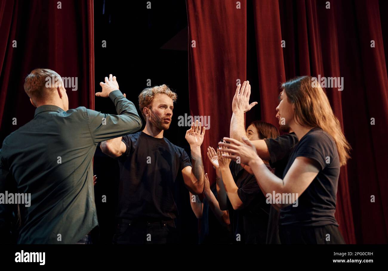 Giving high five, celebrating success. Group of actors in dark colored ...