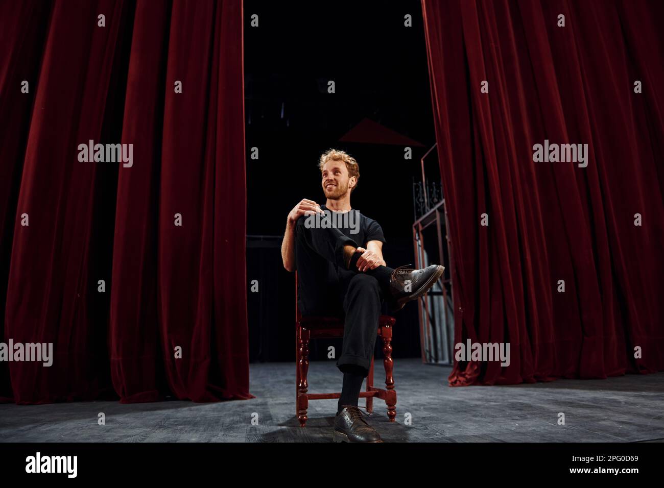 Positive young man sitting on the chair between the curtains on the ...