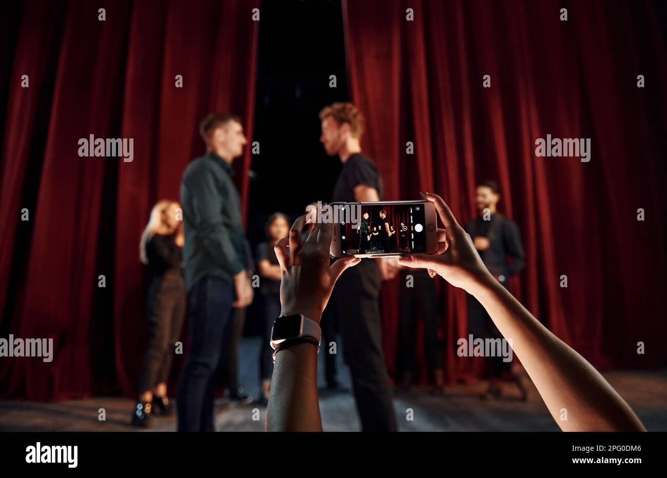 Woman's hands holds phone and taking picture. Group of actors in dark ...