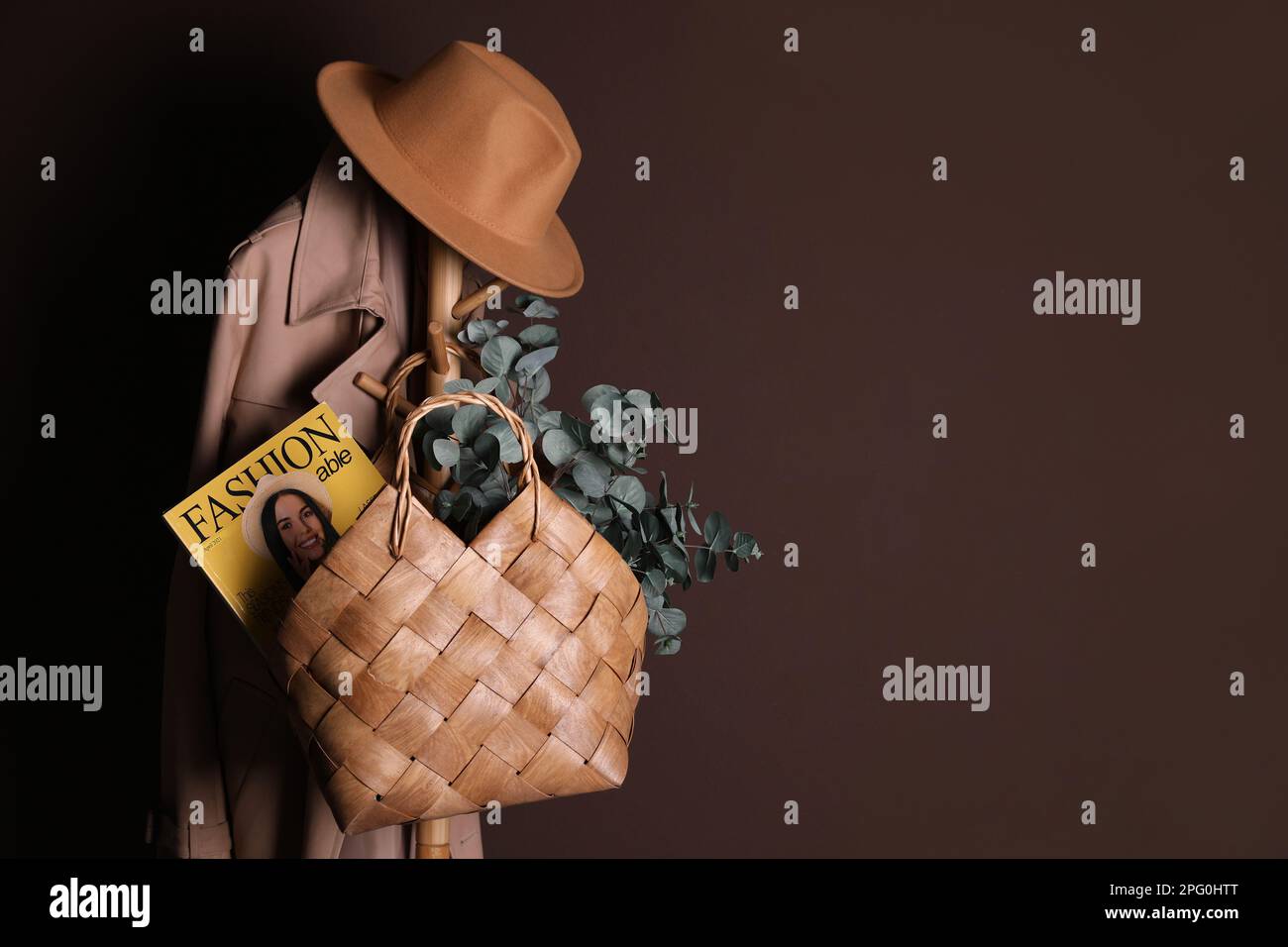 Stylish wicker basket, hat and coat hanging on clothing rack near brown ...