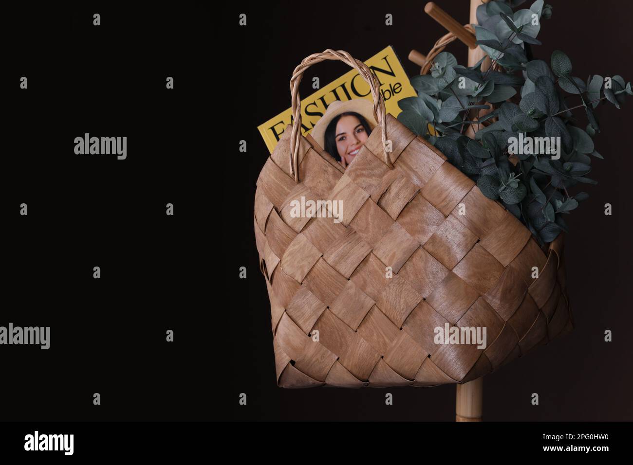 Stylish wicker basket with green plant and magazine hanging on clothing ...