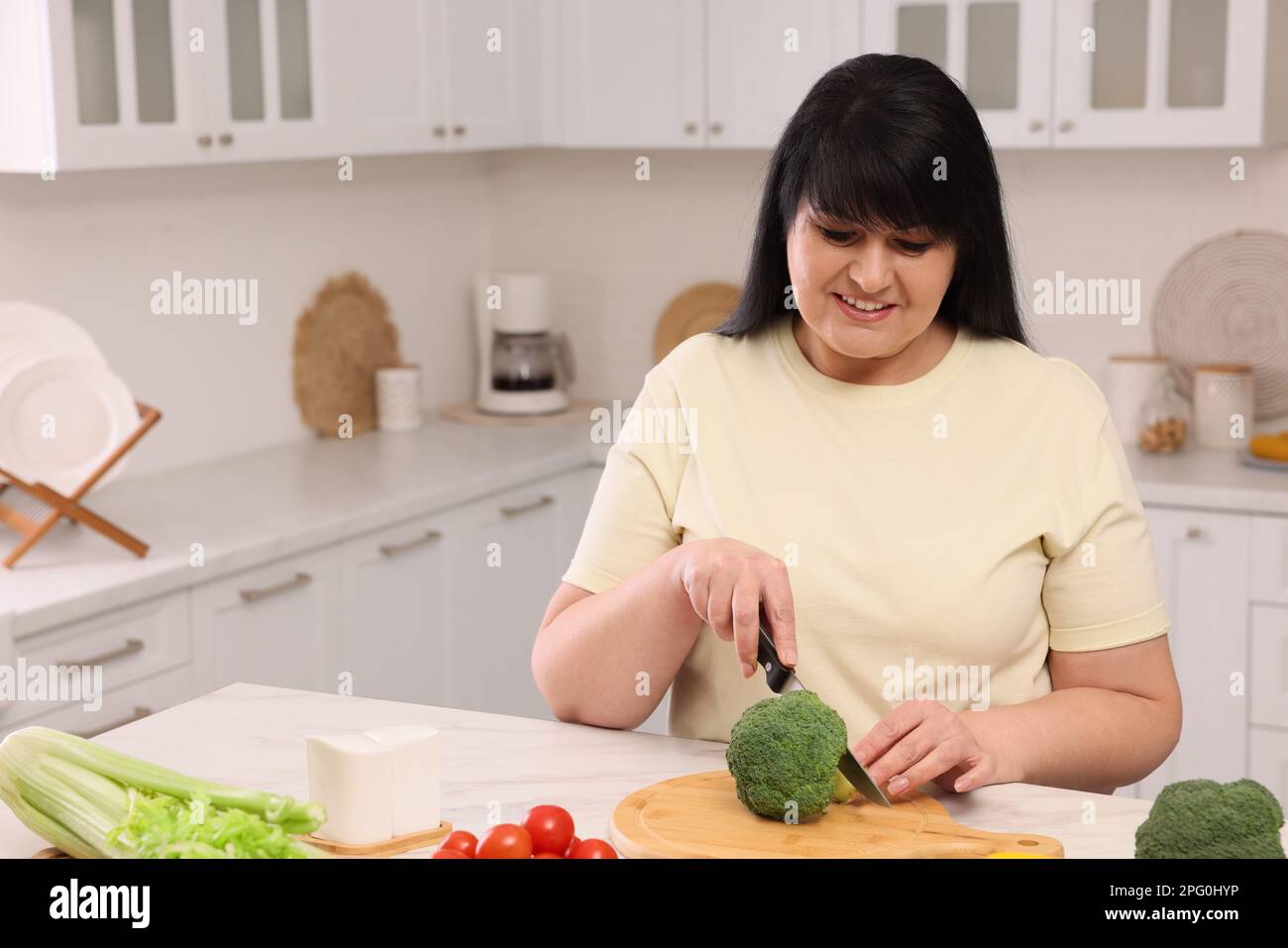 Beautiful overweight woman preparing healthy meal at table in kitchen ...