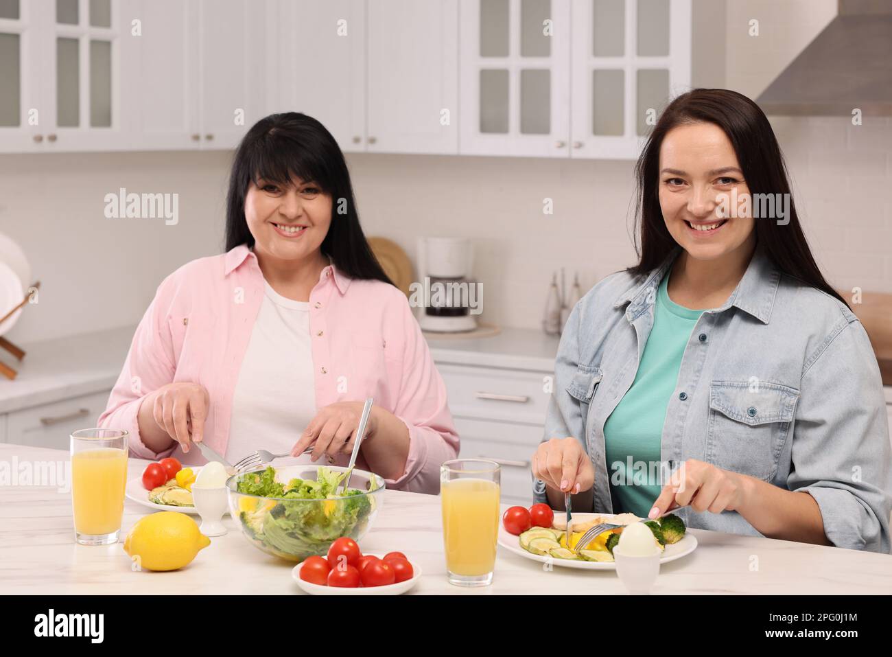 Happy overweight women having healthy meal together at table in kitchen ...