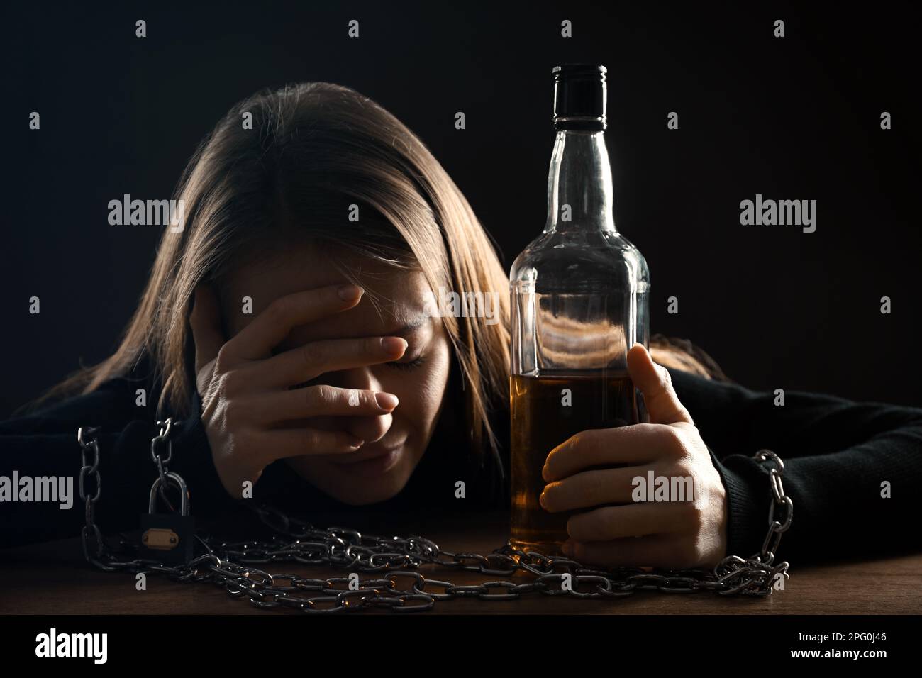 Alcohol addiction. Woman chained with bottle of whiskey at wooden table ...