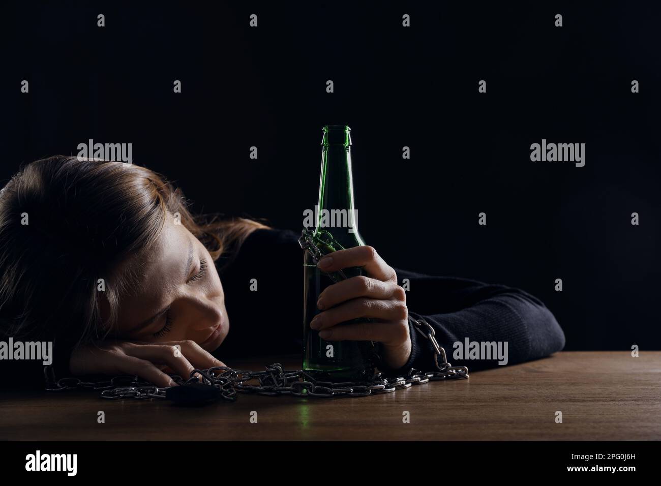 Alcohol addiction. Woman chained with bottle of beer sleeping at wooden ...
