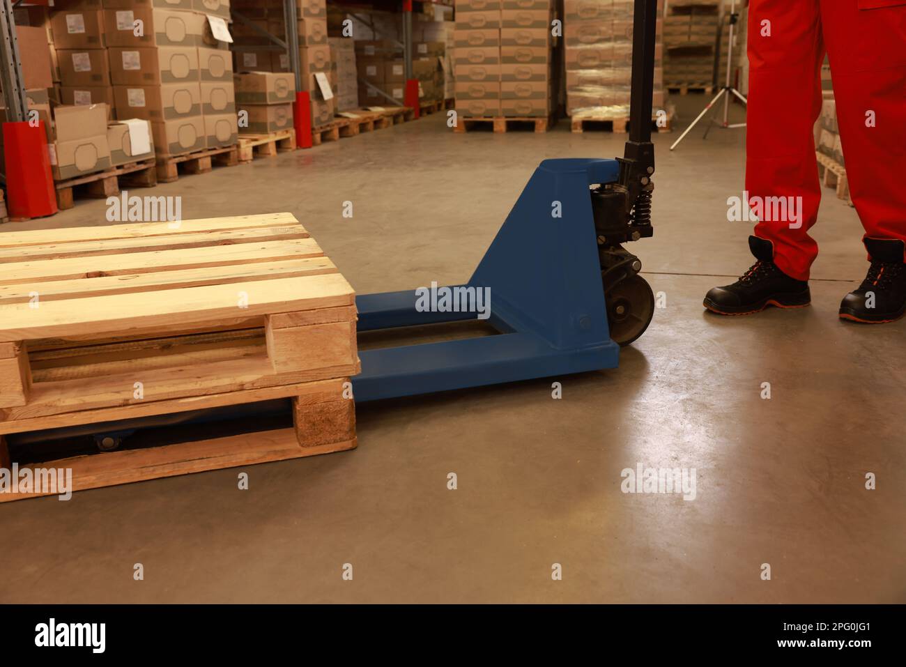 Worker moving wooden pallets with manual forklift in warehouse, closeup ...