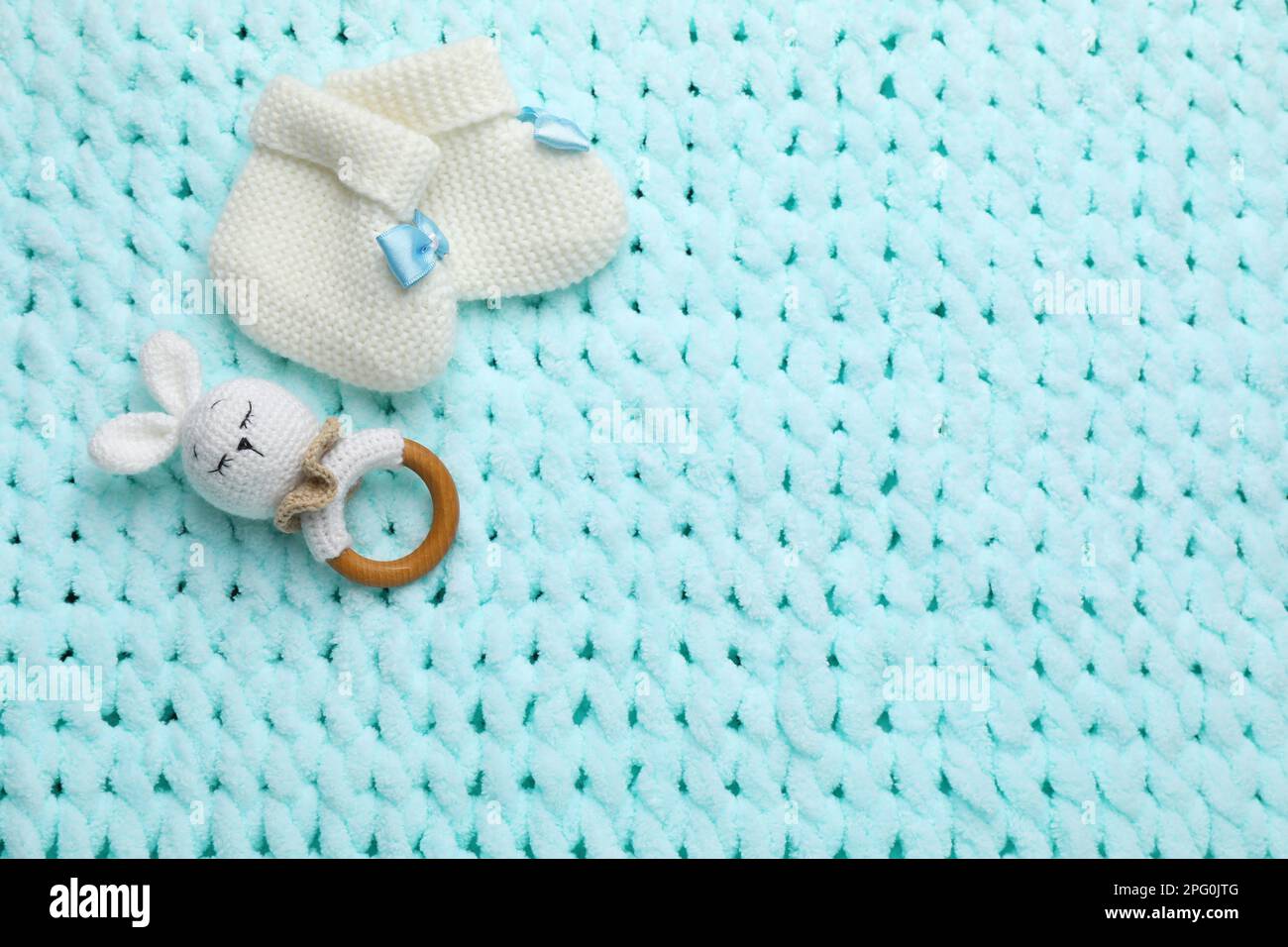 Cute baby booties and toy on light blue knitted fabric, flat lay. Space ...