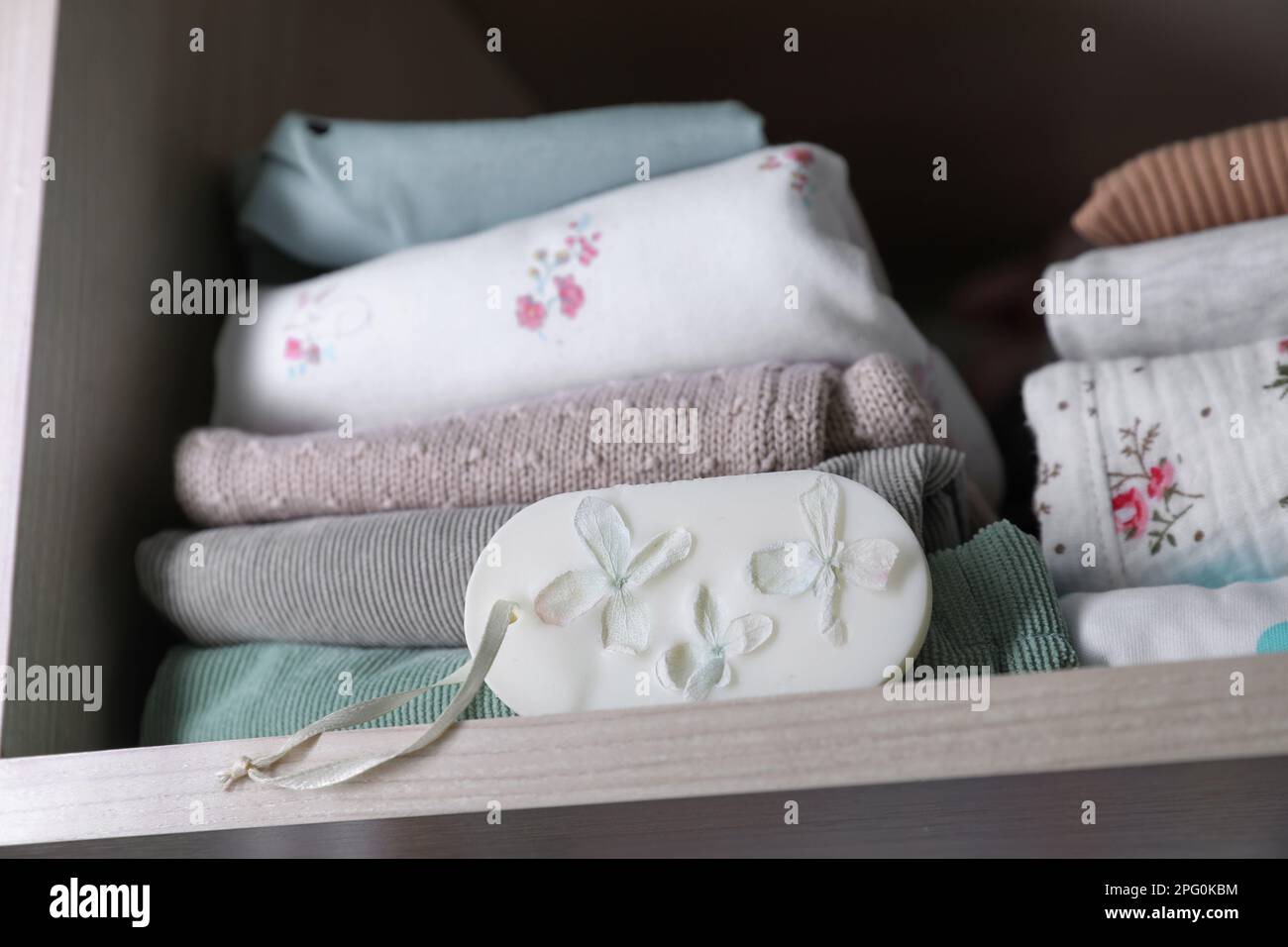 Beautiful scented wax sachet near stack of clothes on shelf in wardrobe ...