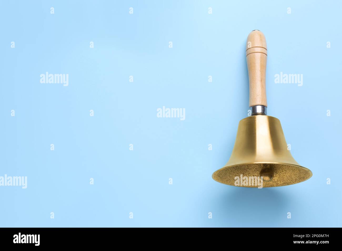 Golden school bell with wooden handle on light blue background, top ...