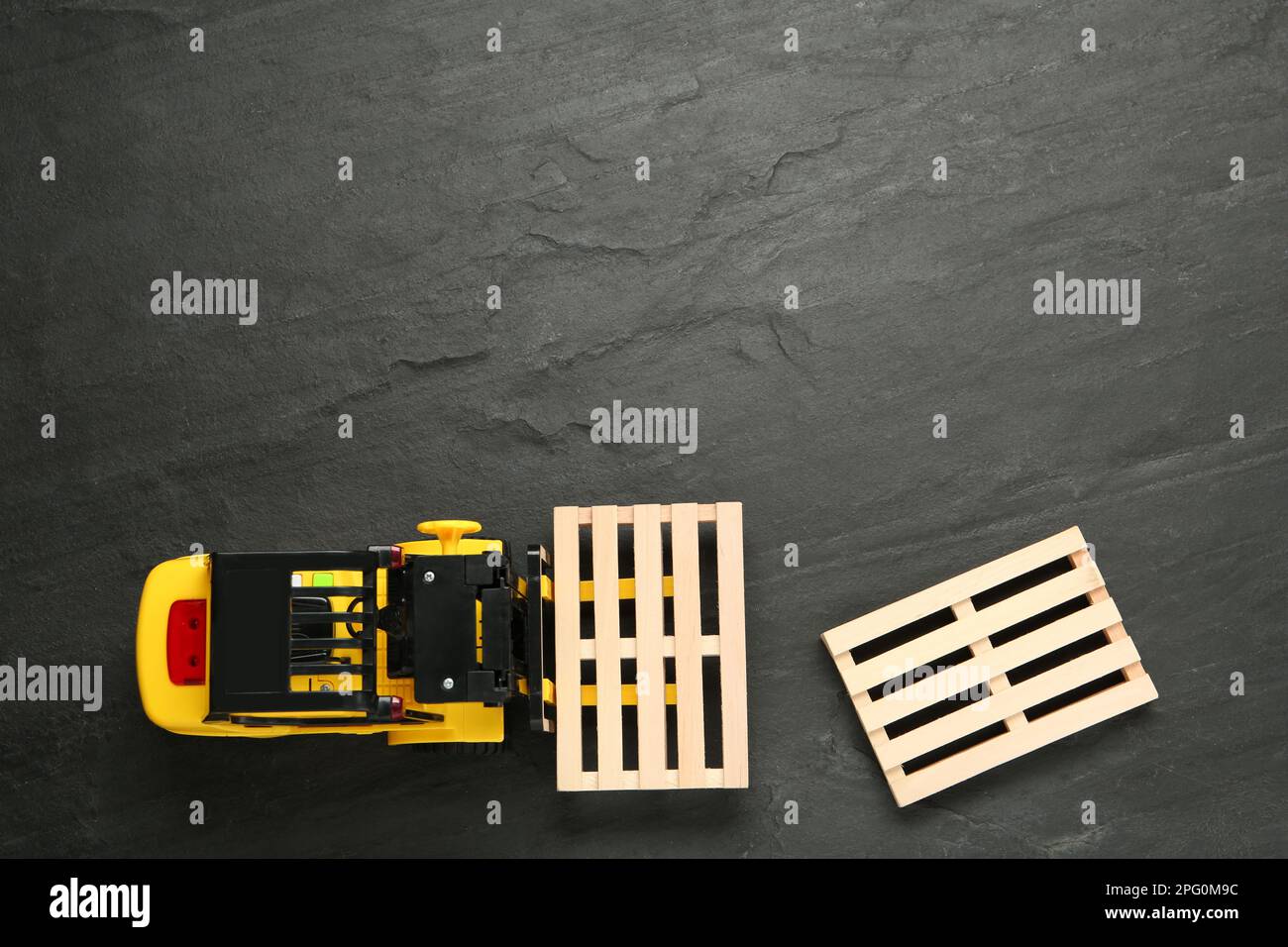 Toy forklift and wooden pallets on black table, flat lay. Space for ...