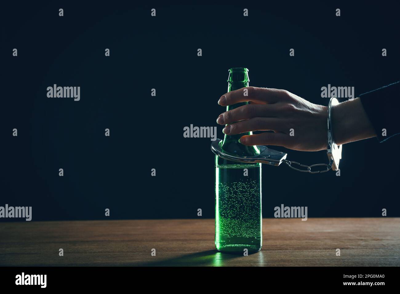 Alcohol addiction. Woman handcuffed to bottle of beer against black ...