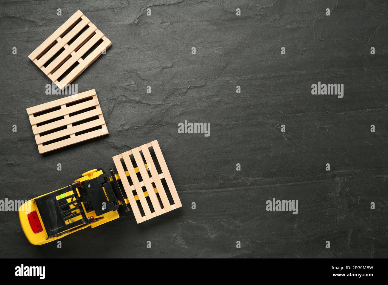 Toy forklift and wooden pallets on black table, flat lay. Space for ...