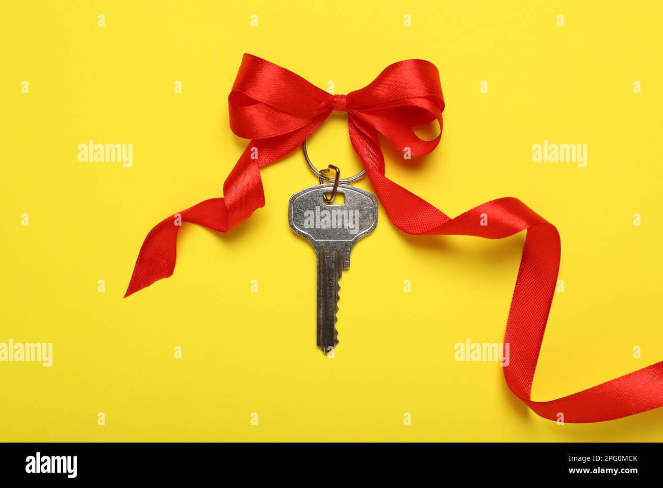 Key with red bow on yellow background, top view. Housewarming party ...