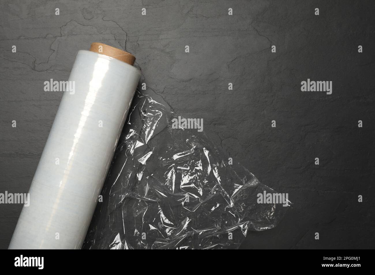Roll of plastic stretch wrap film on black table, top view. Space for ...