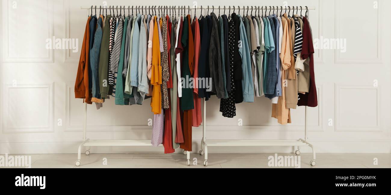 Racks with stylish clothes near white wall indoors, banner design. Fast ...
