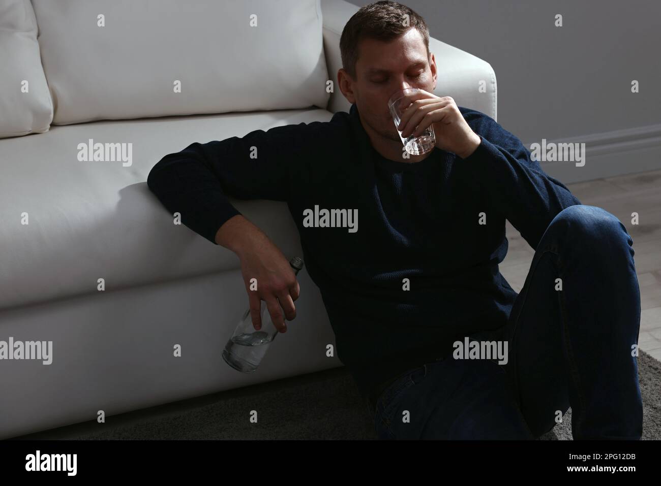 Addicted man drinking alcohol near sofa indoors Stock Photo - Alamy