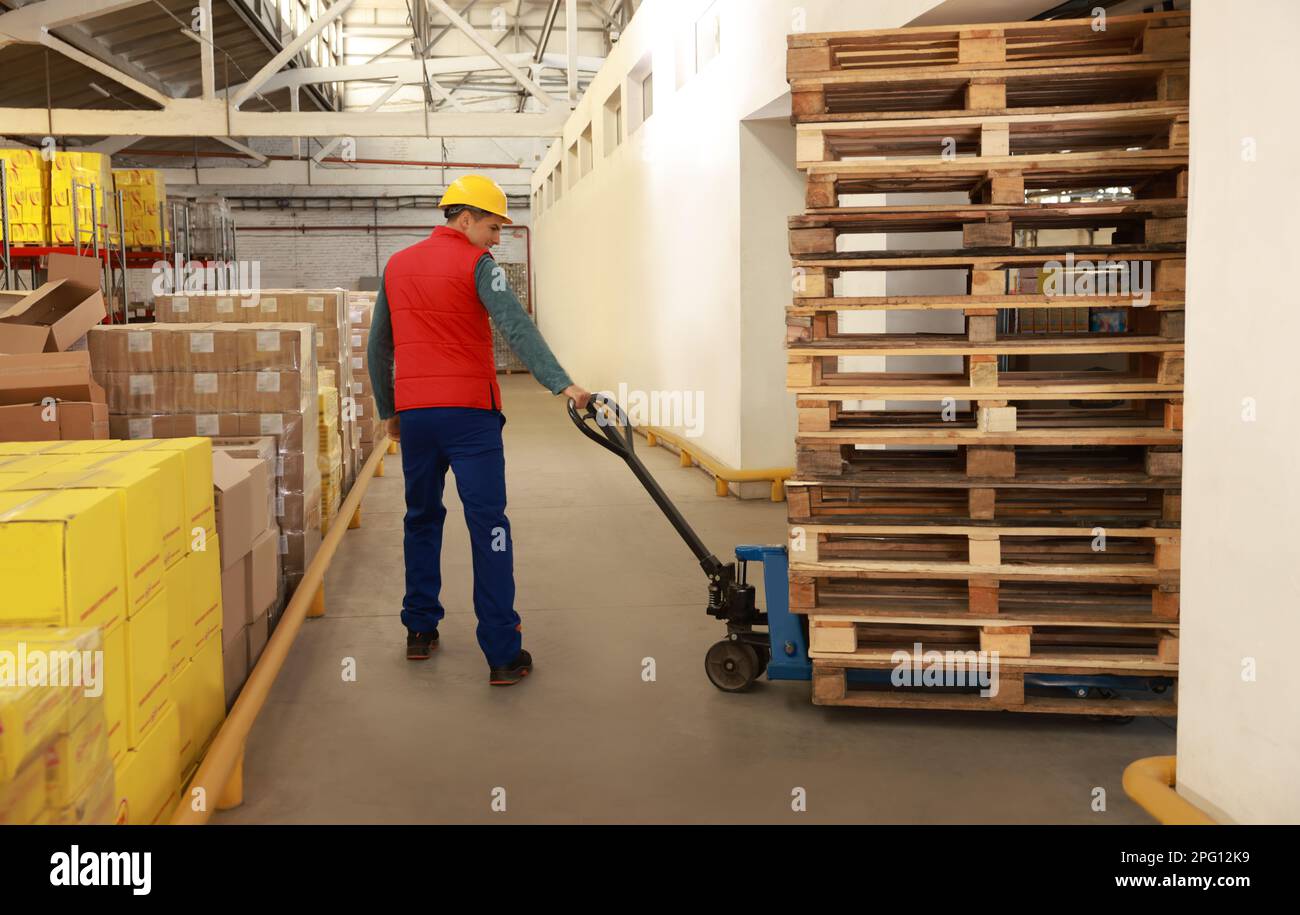 Worker moving wooden pallets with manual forklift in warehouse Stock ...