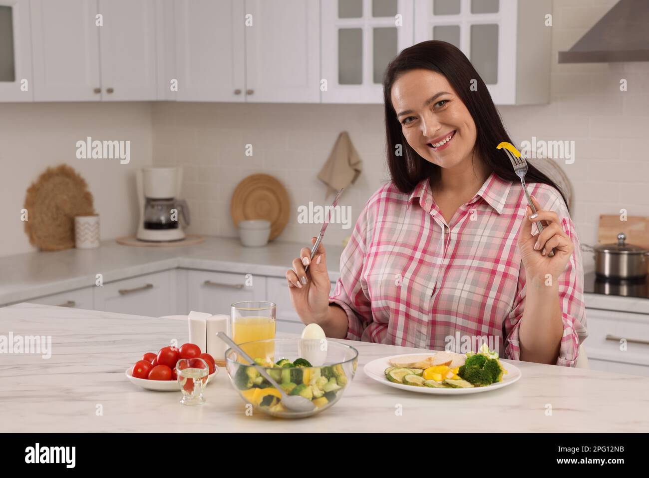 Beautiful overweight woman having healthy meal at table in kitchen ...