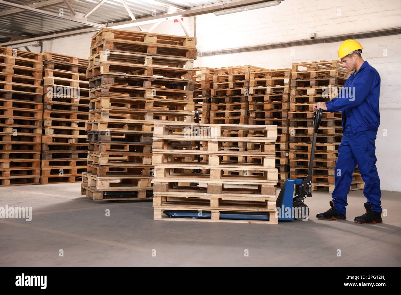 Worker moving wooden pallets with manual forklift in warehouse Stock ...