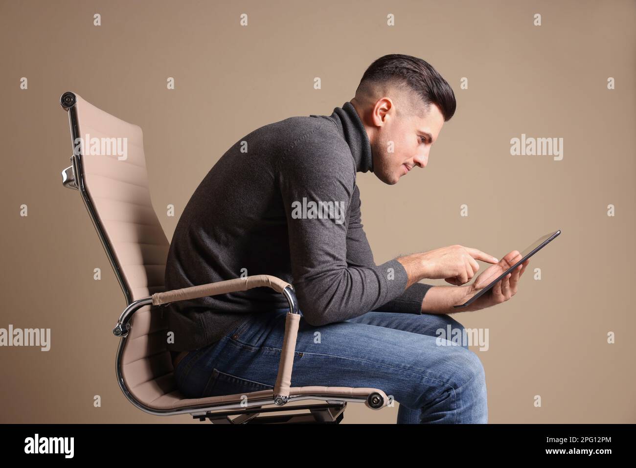 Man with poor posture using tablet while sitting on chair against beige ...