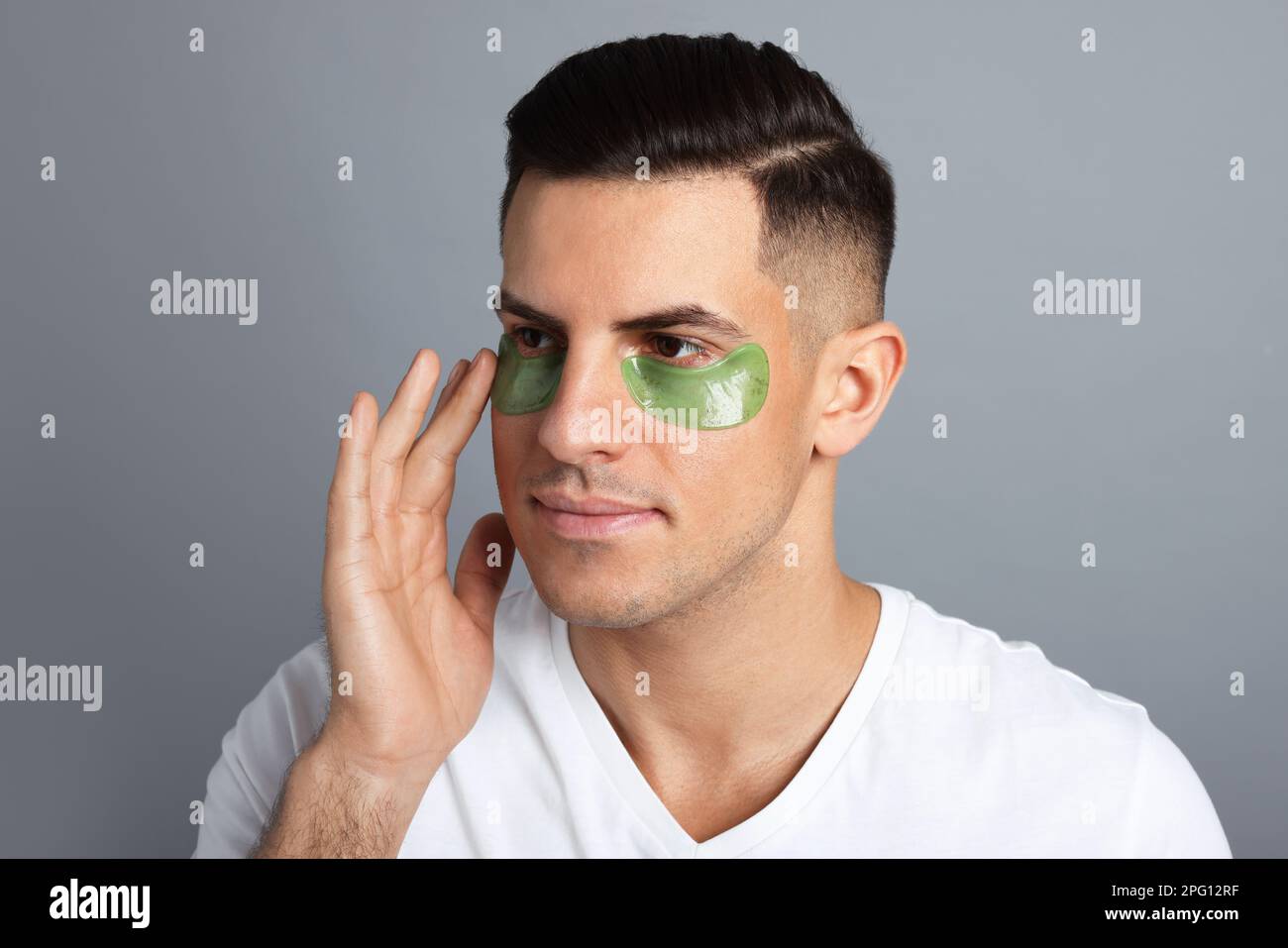 Man applying green under eye patch on grey background Stock Photo - Alamy