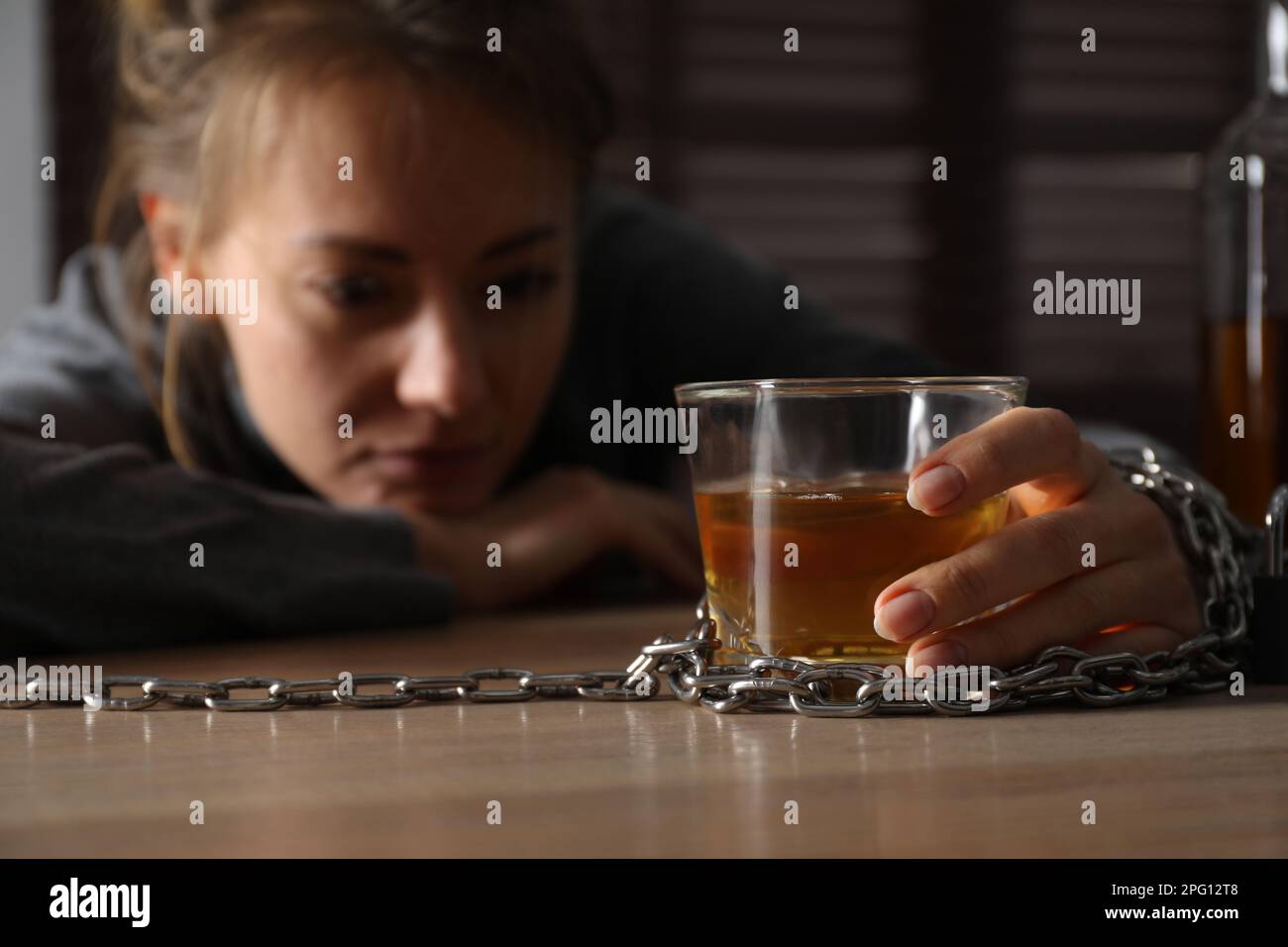 Alcohol addiction. Woman chained with glass of liquor at wooden table ...