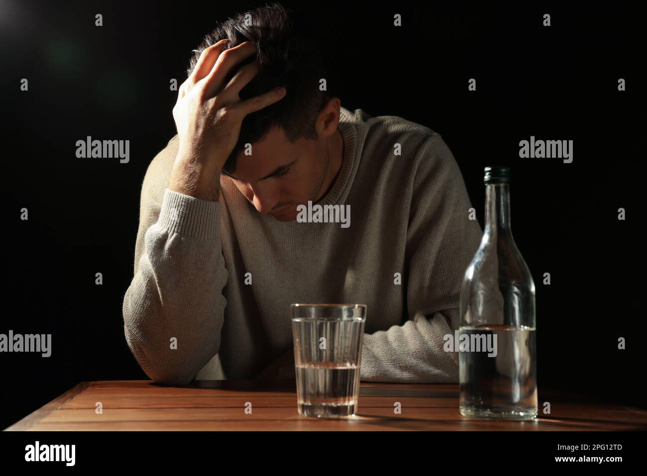 Addicted man with alcoholic drink at wooden table against black ...