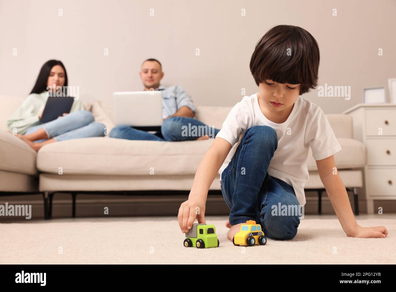 Child playing with toys and parents working on sofa at home Stock Photo ...
