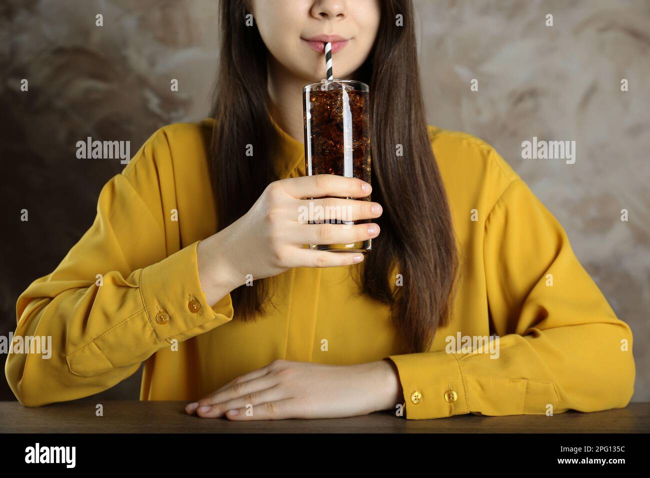 Woman drinking cola with ice at wooden table against grey background ...