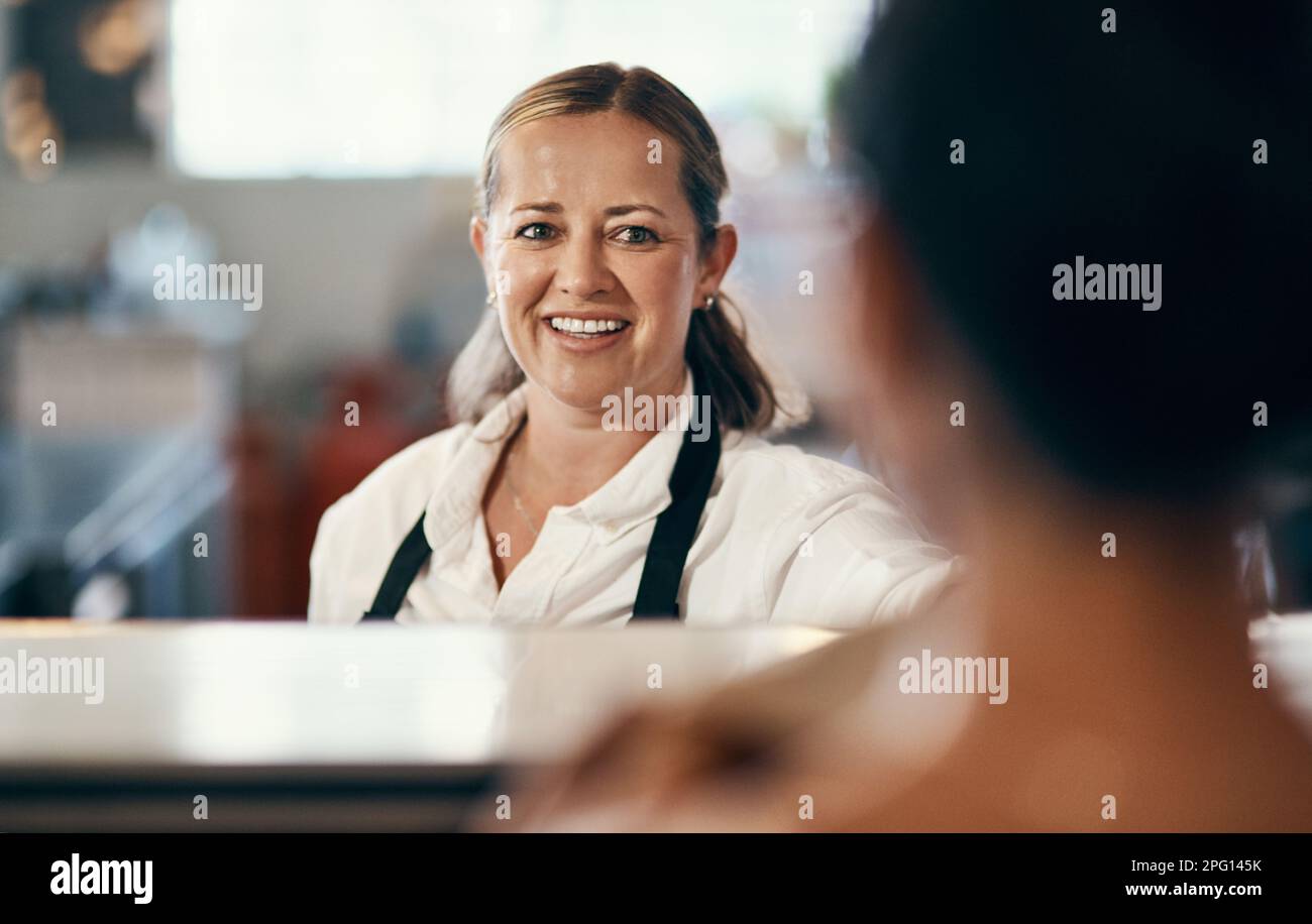 A friendly smile speaks volumes. a mature barista serving a customer at ...