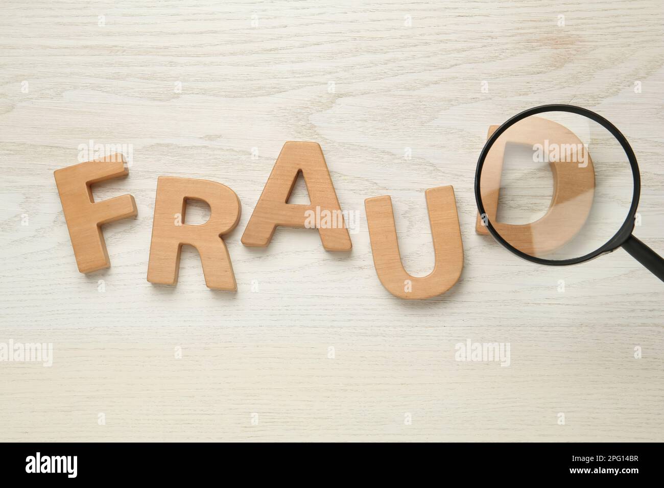Word Fraud made of wooden letters under magnifying glass on white ...