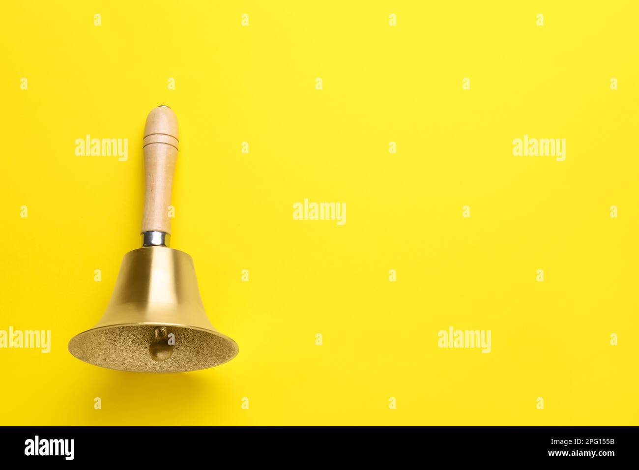 Golden school bell with wooden handle on yellow background, top view ...