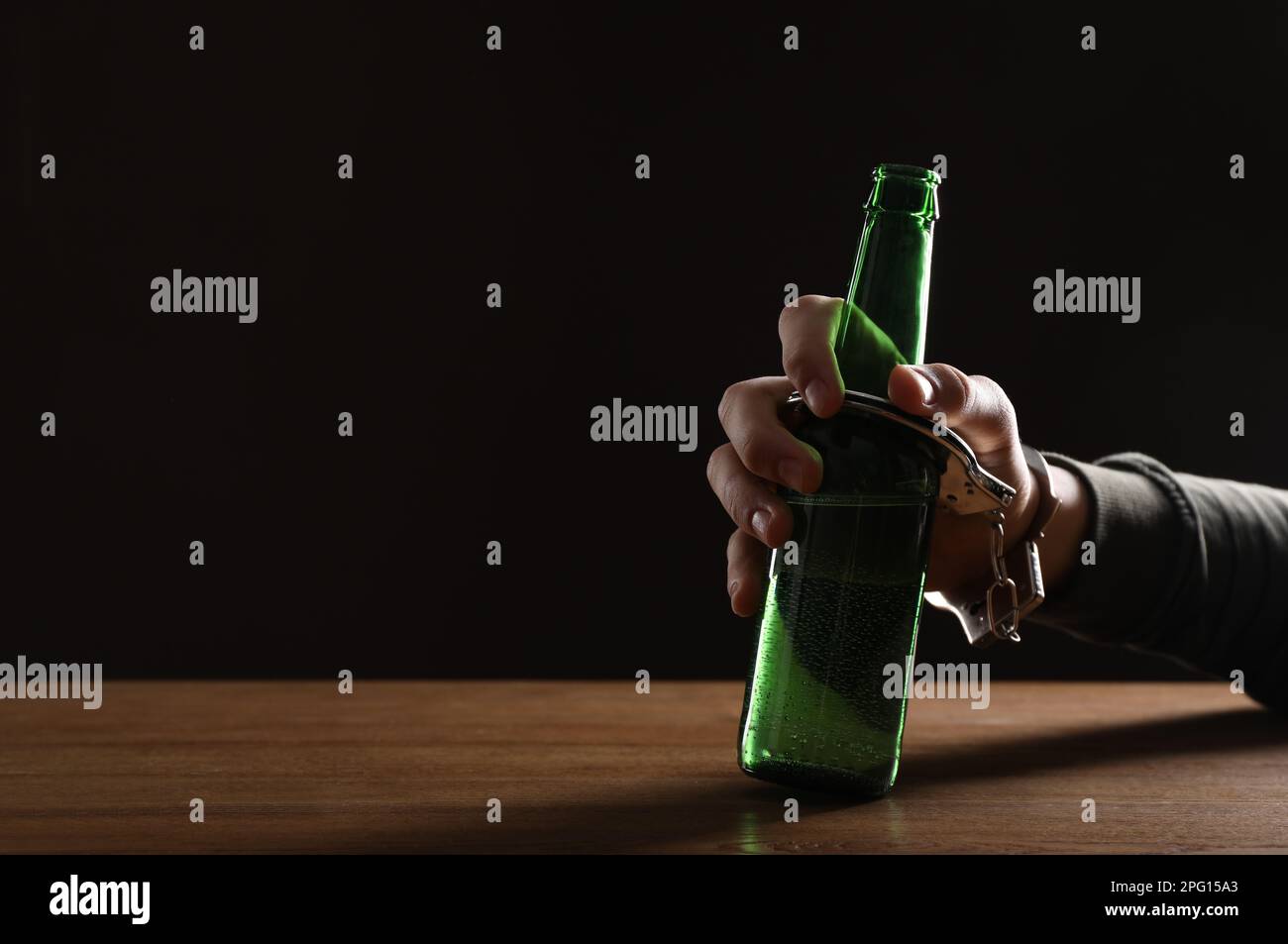 Alcohol addiction. Man handcuffed to bottle of beer at wooden table ...