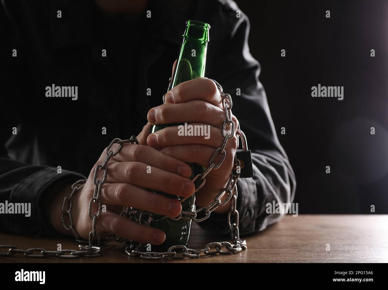 Alcohol addiction. Man chained with bottle of beer at wooden table ...