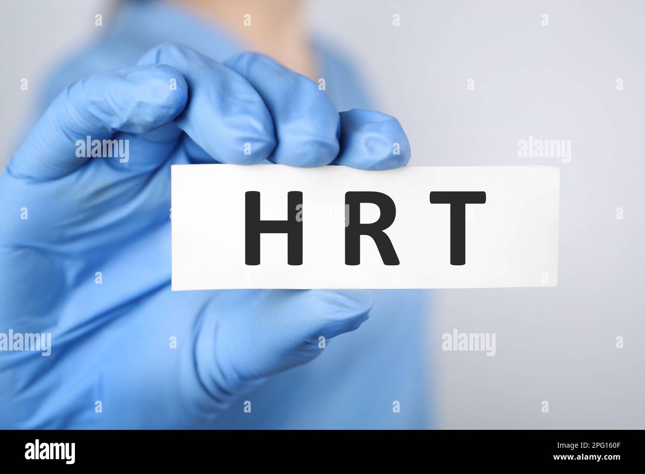 Doctor holding card with abbreviation HRT on light grey background ...