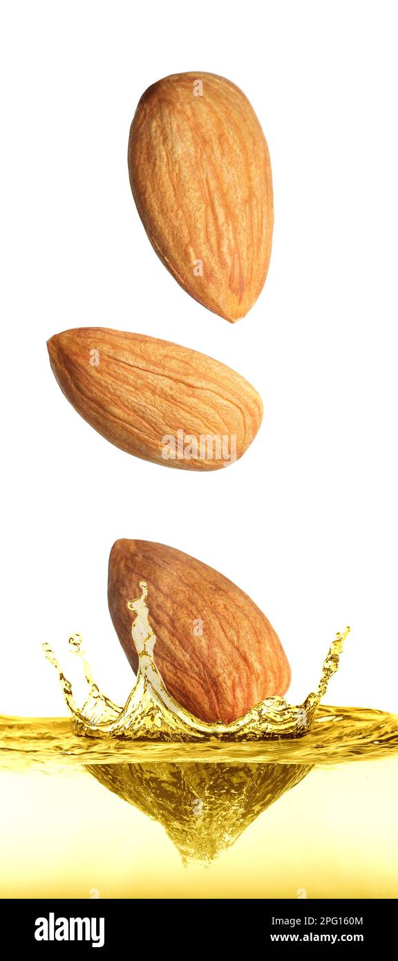 Tasty nuts falling into organic almond oil on white background ...