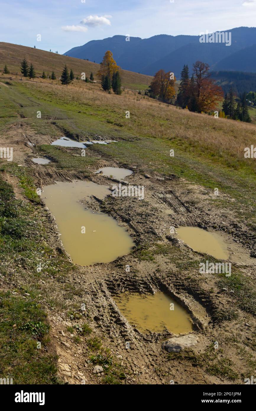 Vanishing dirt road with deep rut and puddles in village at sunset ...