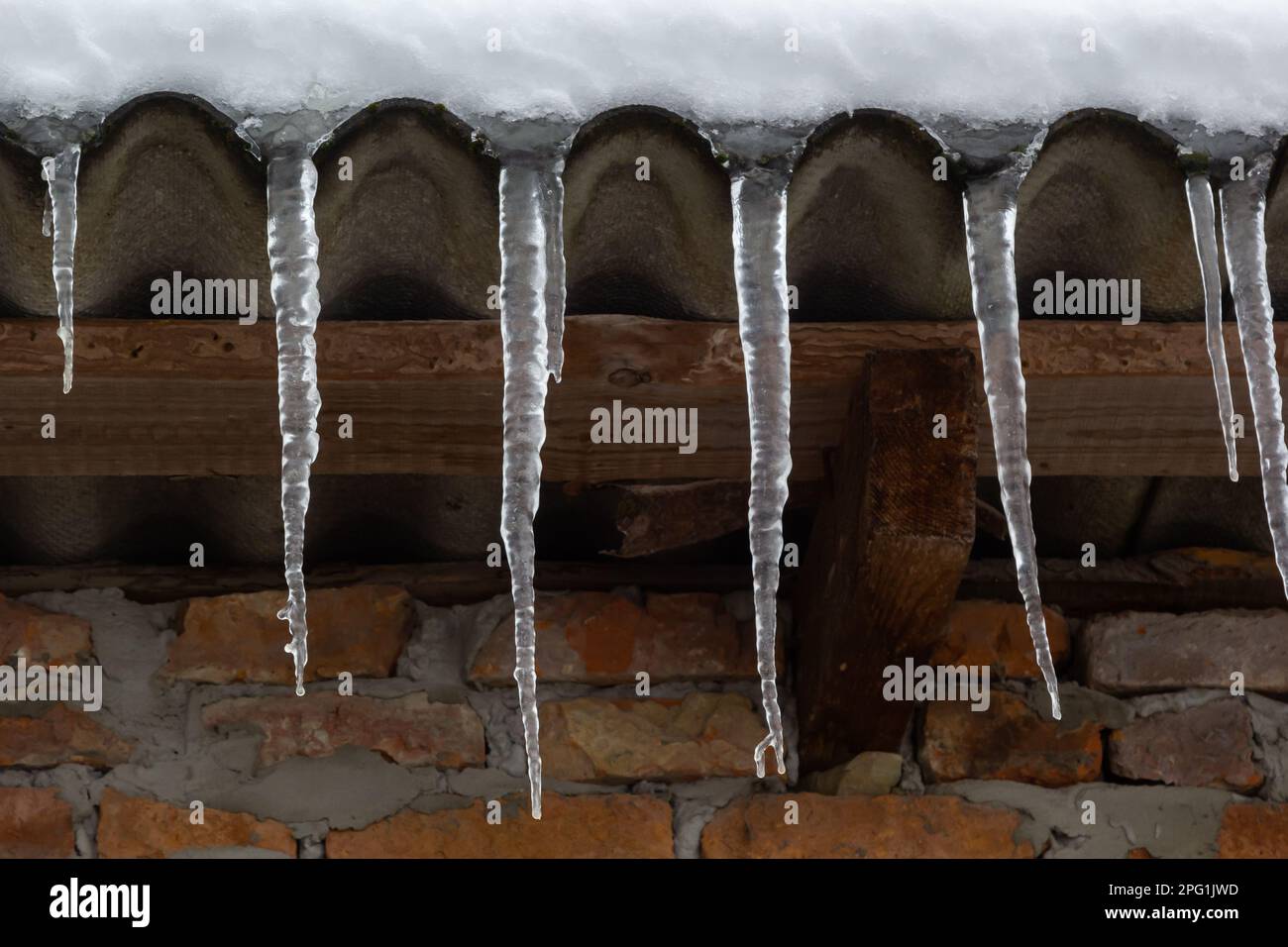 Sharp icicles and melted snow hanging from the eaves of the roof ...