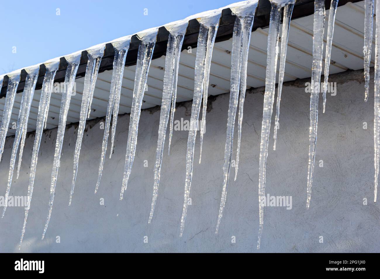 Sharp icicles and melted snow hanging from eaves of roof. Beautiful transparent icicles slowly ...