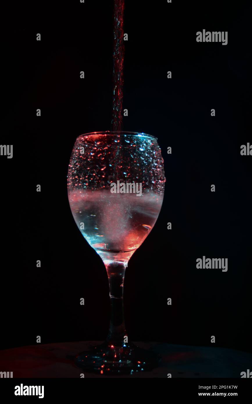 Wine glass filling with liquid on a black background, long exposure ...