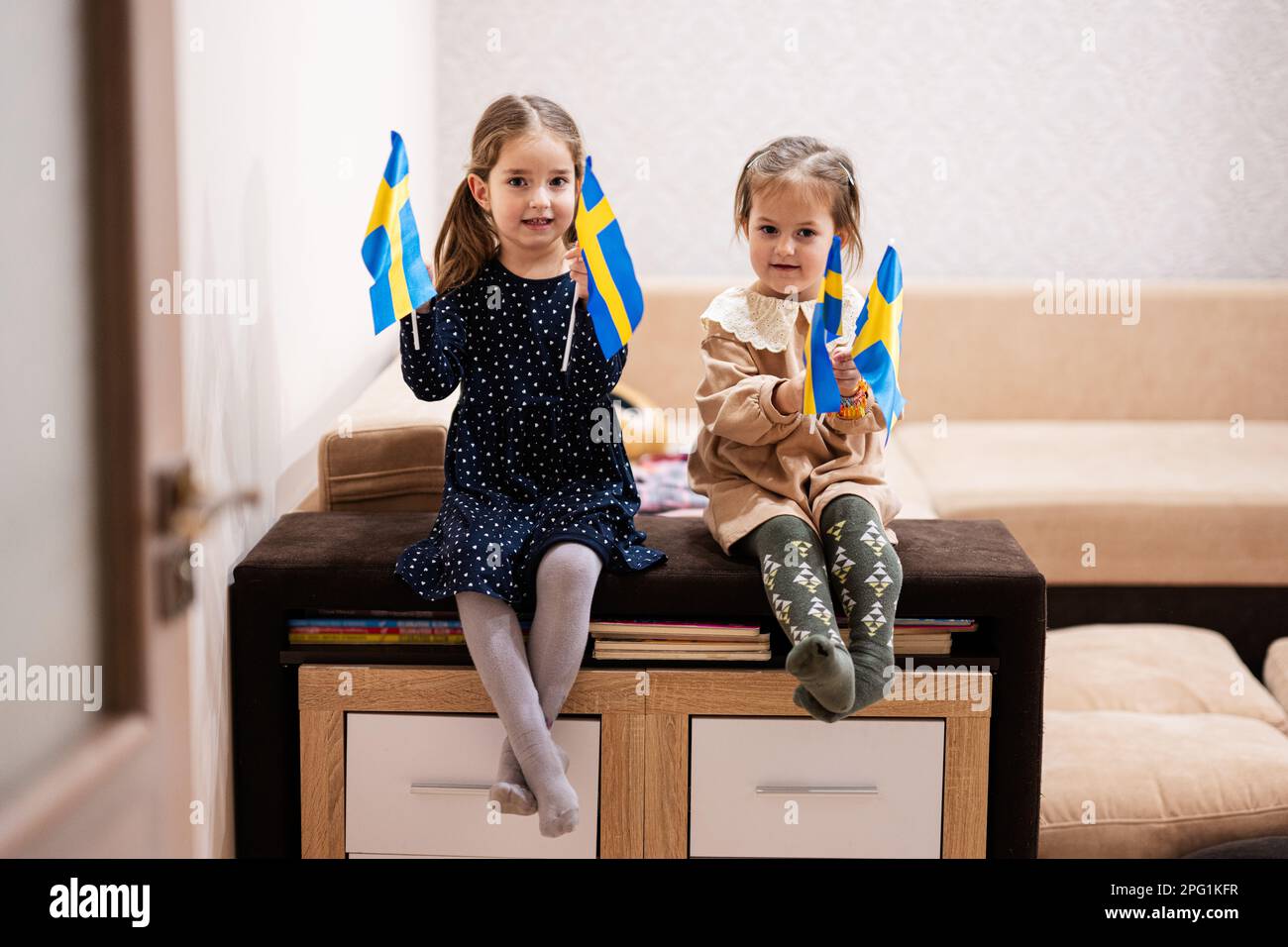 Two sisters are sitting on a couch at home with swedish flags on hands ...