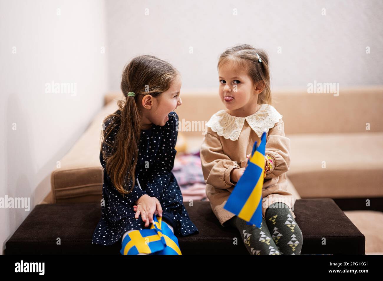 Two sisters are sitting on a couch at home with swedish flags on hands ...