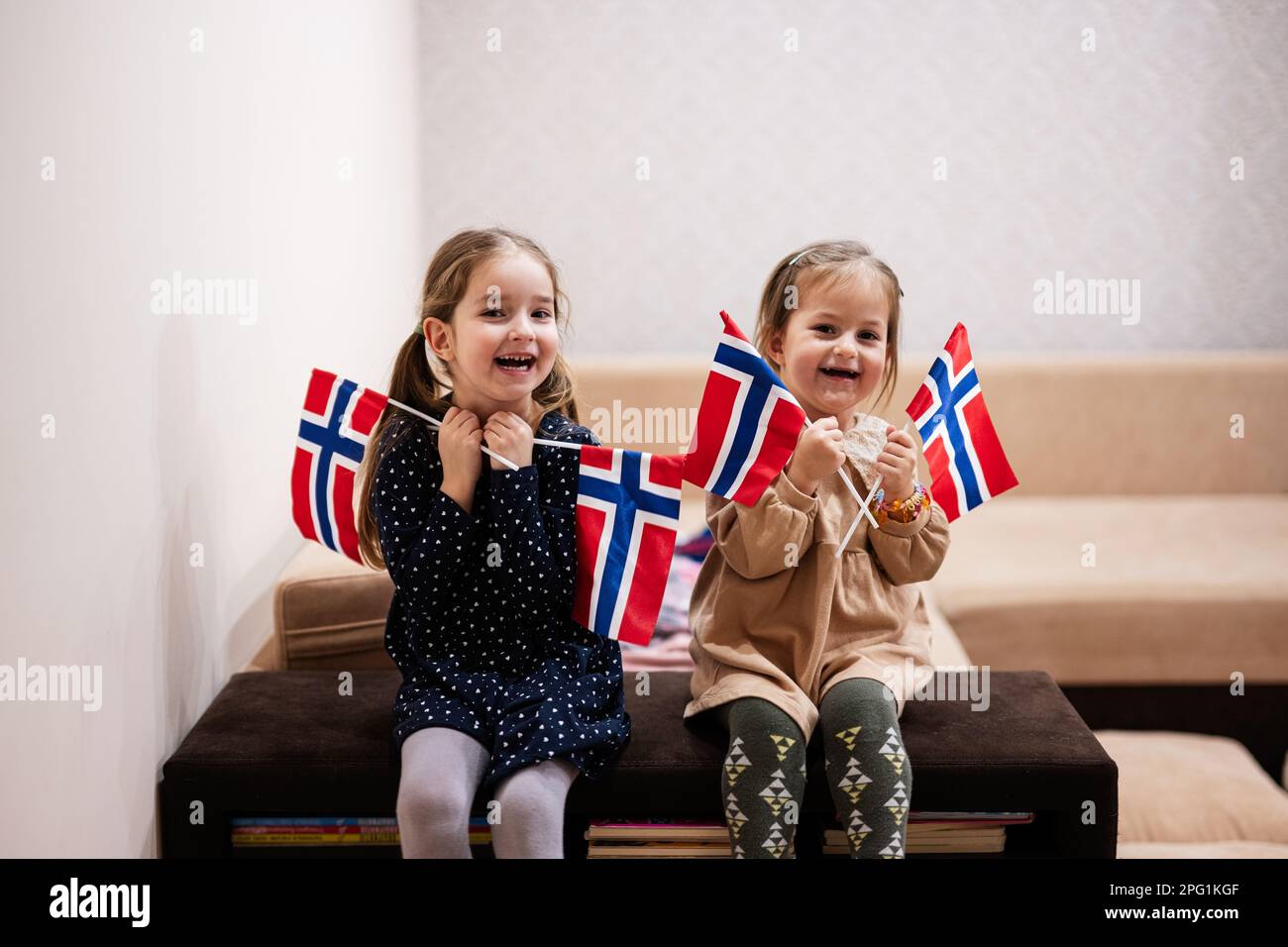 Two sisters are sitting on a couch at home with norwegian flags on ...