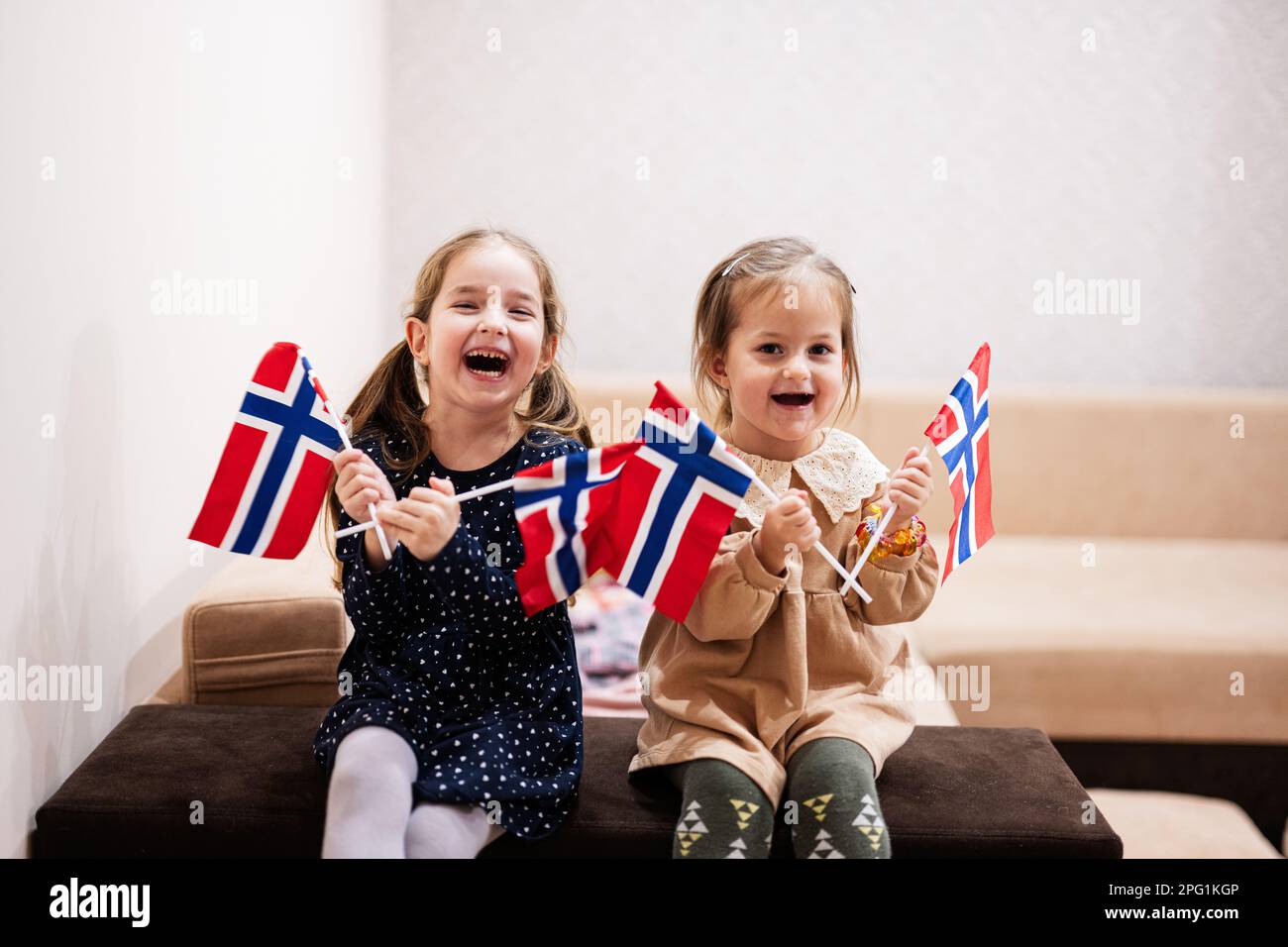 Two sisters are sitting on a couch at home with norwegian flags on ...