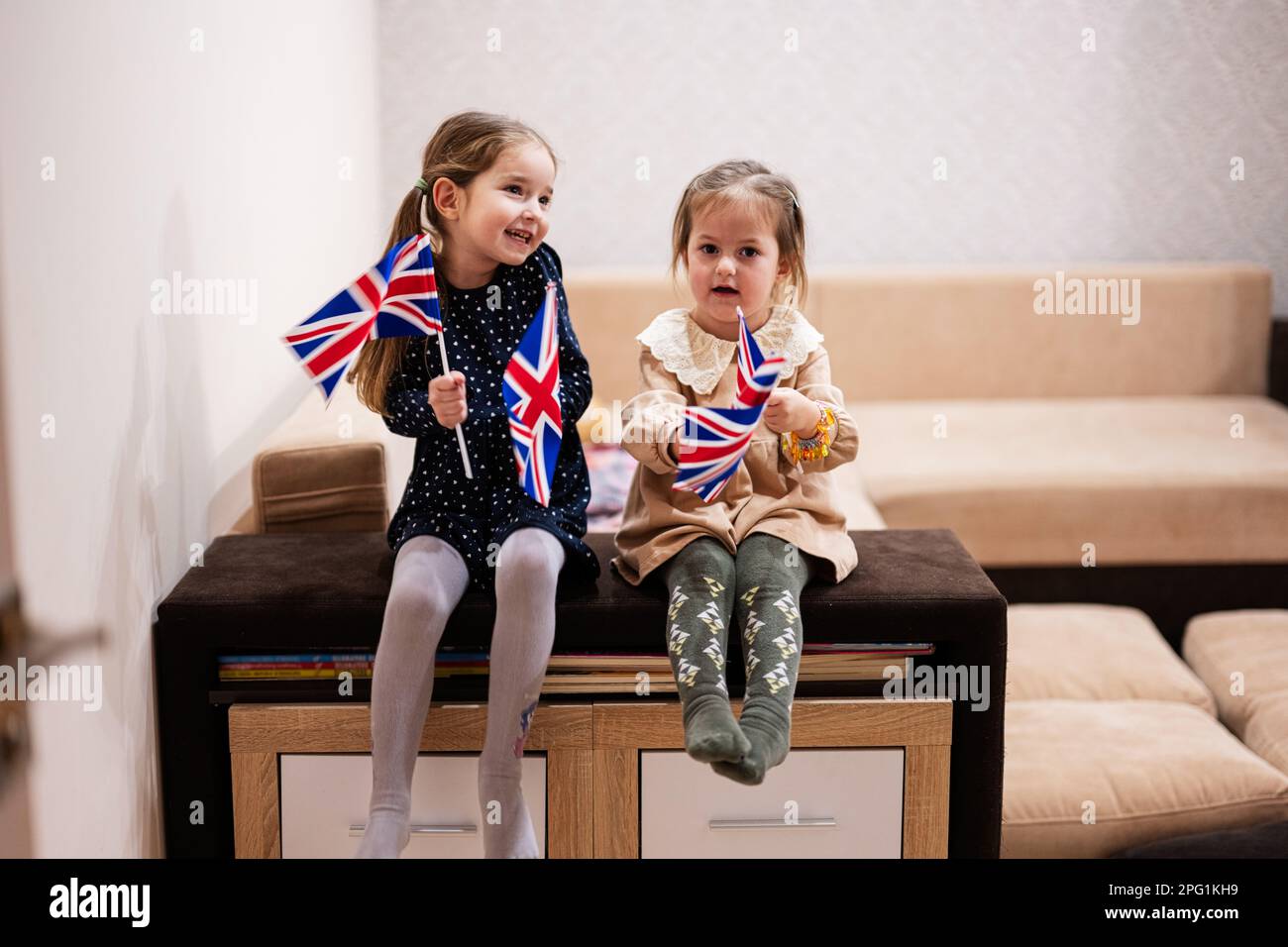Two sisters are sitting on a couch at home with british flags on hands ...