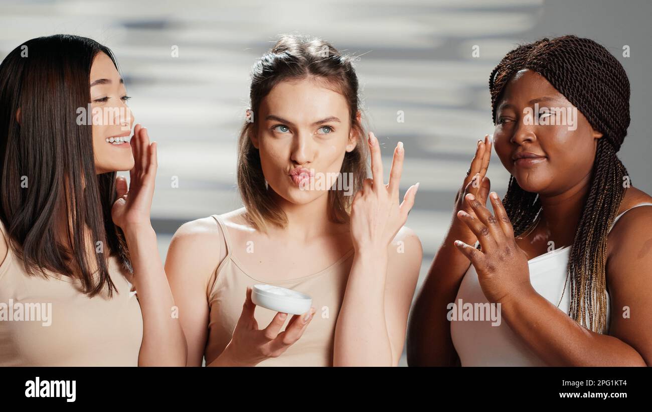 Interracial women applying moisturizing face cream, using skincare ...