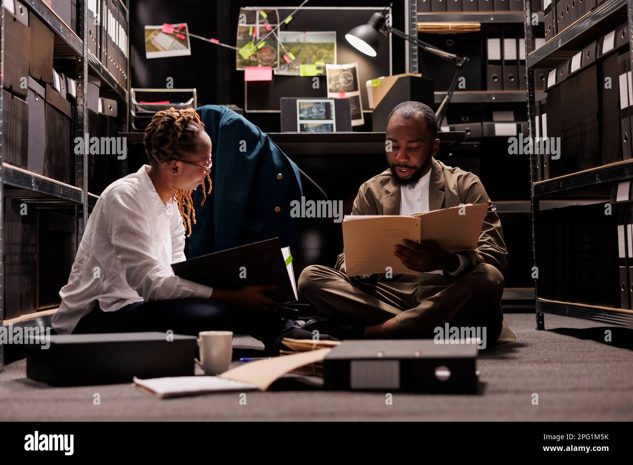 Police detective partners sitting on floor surrounded by case files ...