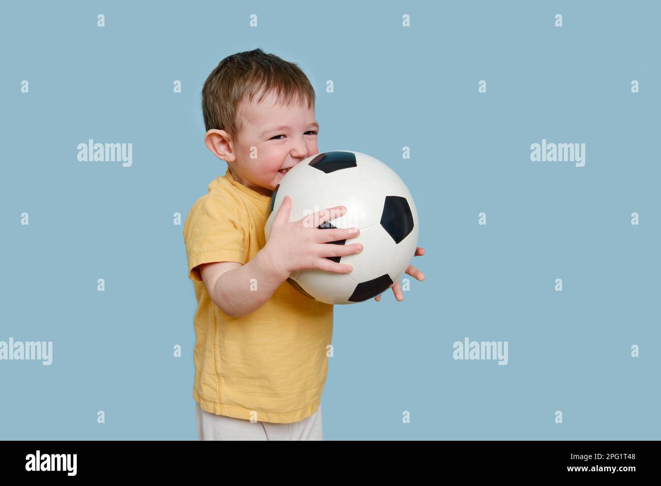Happy toddler baby with a soccer ball on a studio blue background ...